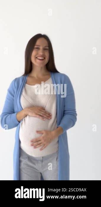 Portrait of a friendly, smiling pregnant woman gently caressing belly ...