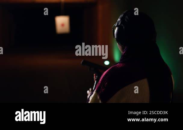 Portrait of joyous shooting range customer shooting targets with pistol, learning to operate ...