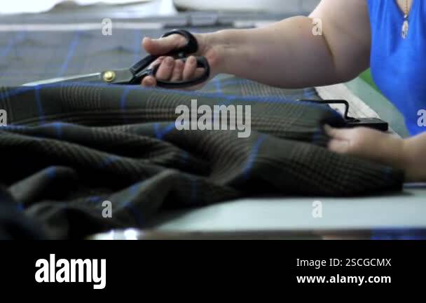A woman tailor cuts fabric with scissors. A garment factory worker cuts ...