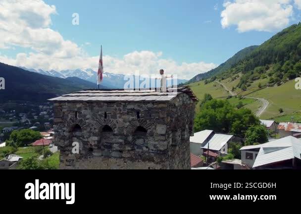 Young tourist standing with open arms on roof of typical Svanetian tower in Mestia, Svaneti ...