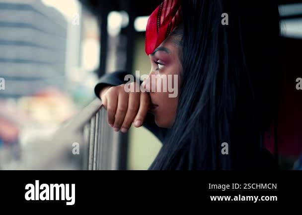 One contemplative young black woman gazing at view from balcony window in deep mental reflection ...