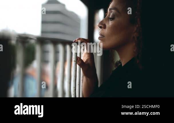 Profile close-up of a serious black woman leaning ln metal bar by home ...