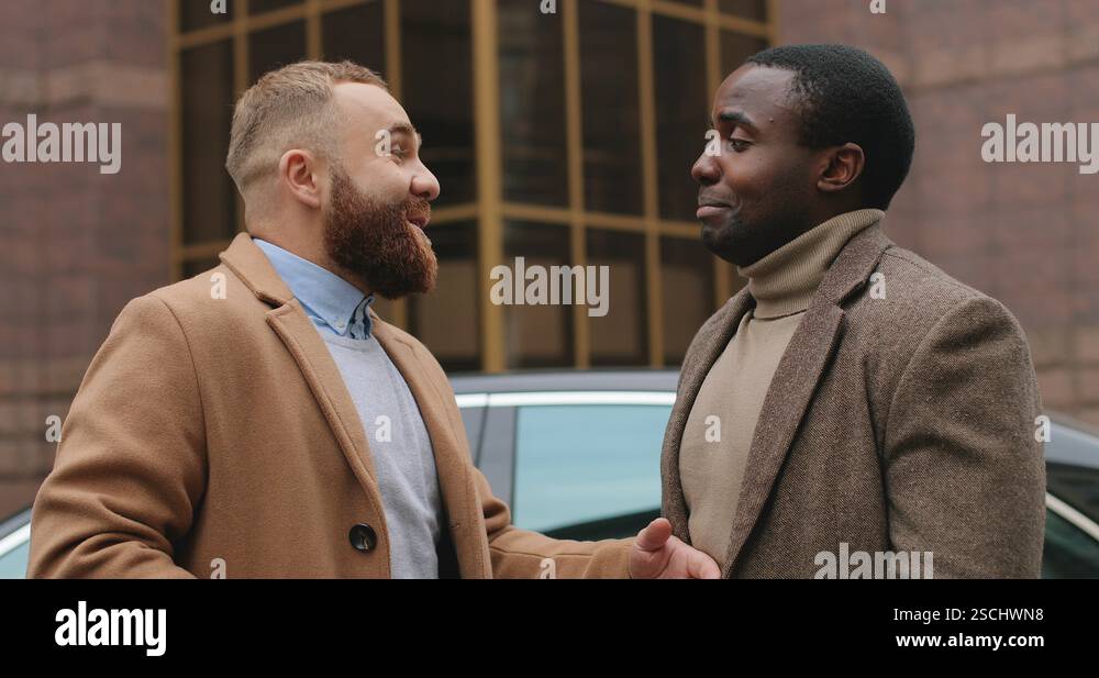 Two mixed-races businessmen in casual coats chatting cheerfully at the ...