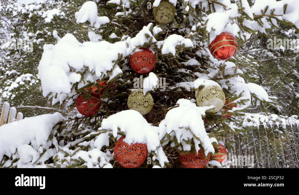 Christmas tree covered with snow, decorated with sparkly toys. Slow ...