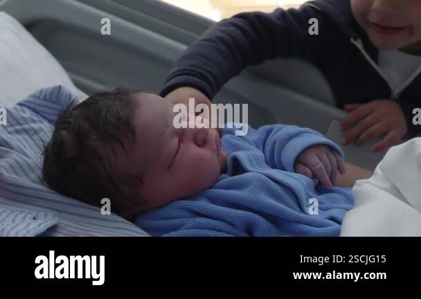 Sibling intercts with newborn baby brother at hospital resting in bed ...