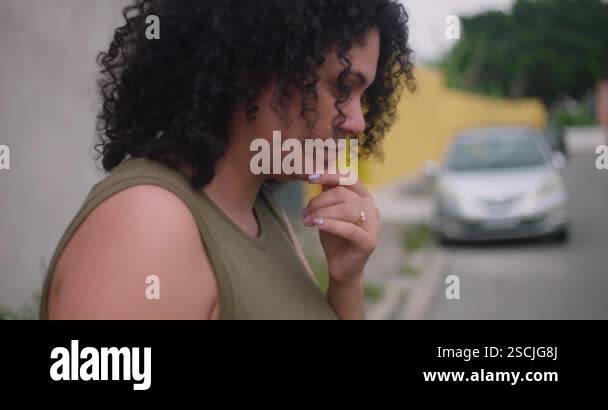 Worried woman standing outdoors with hand on chest, mid-profile view, urban street background ...