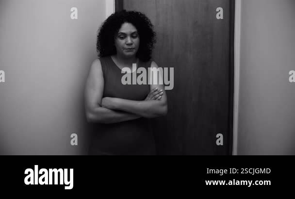 Black and white portrait of a woman leaning against a door, arms crossed, expressing emotional ...