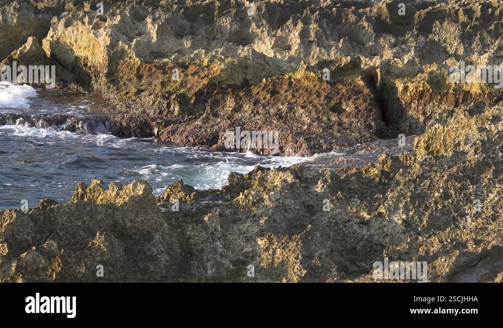 waves crash against the sharp rocks provide a beautiful view on sunset ...