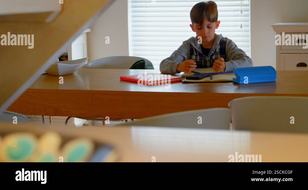 Front view of Caucasian boy doing his homework at dining table in a ...