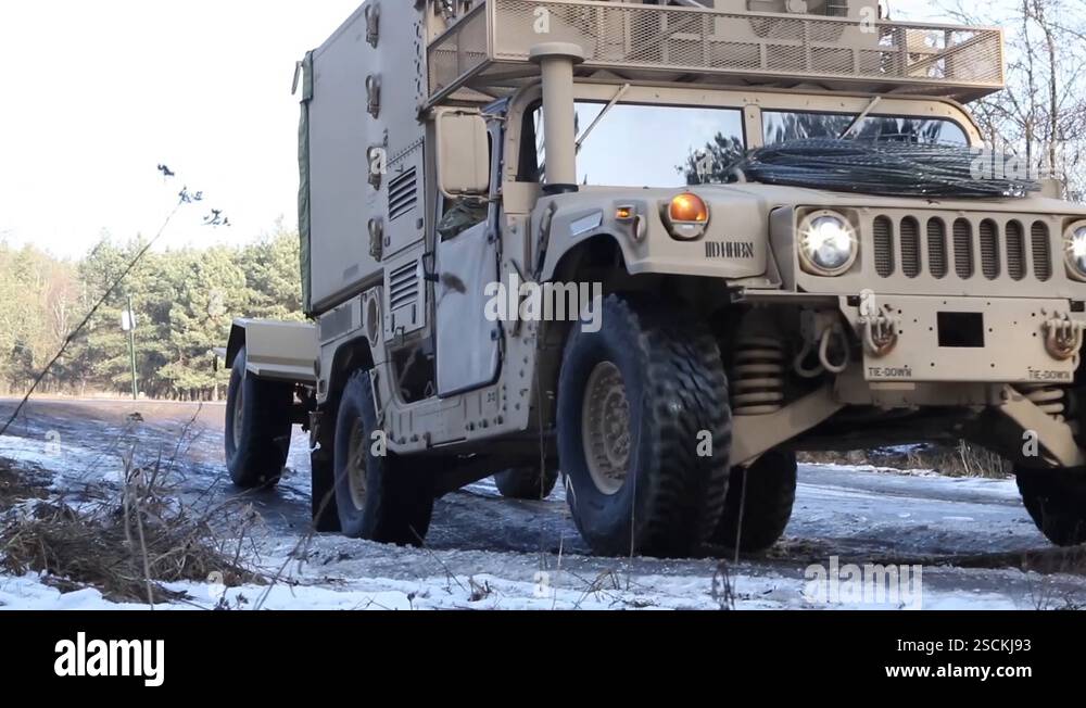 U.S. military vehicle towing trailer driving onto track covered in ice ...