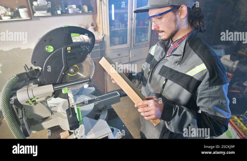 A young carpenter installs a wooden workpiece in a circular sawing ...