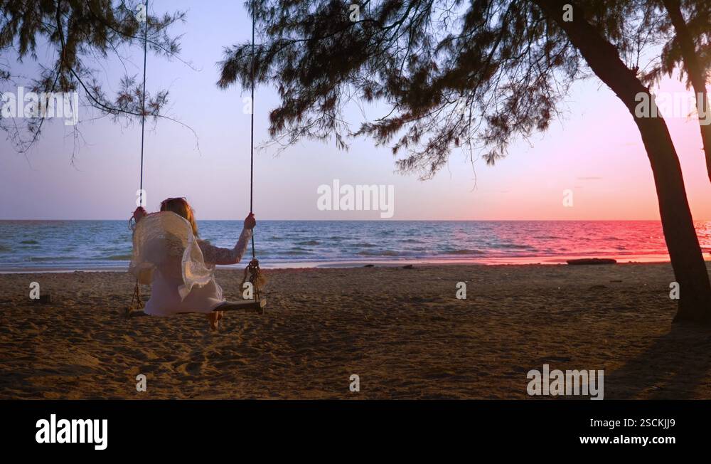 A happy blonde girl in a white dress and lace cape is swinging on a ...