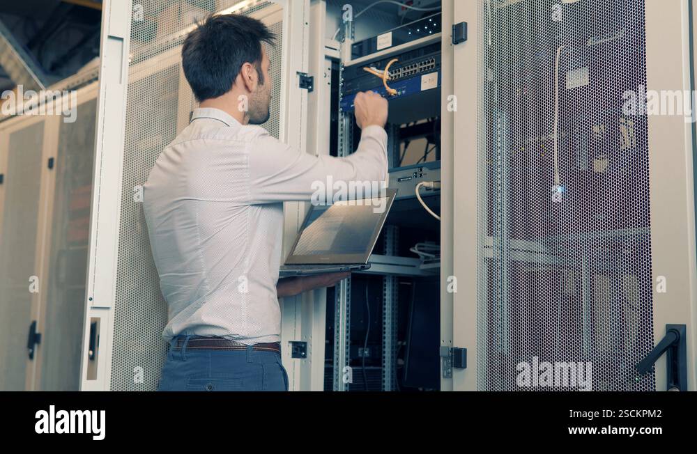 IT Technician Working On A Laptop Standing Before Open Server Rack ...
