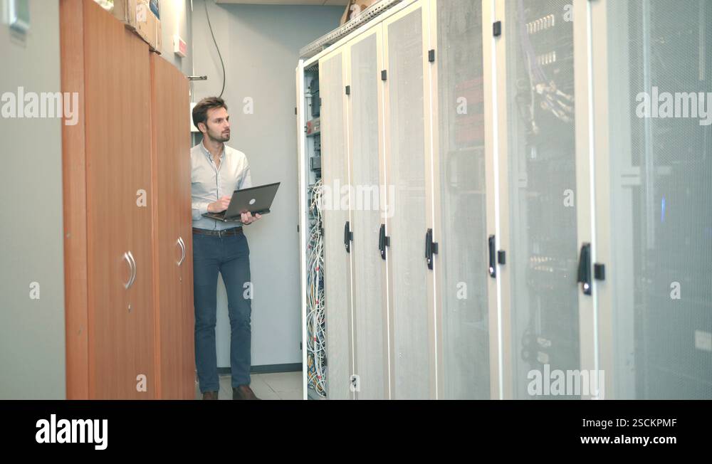 Man Working On Laptop In Server Room Checking Rack Server Cabinet And ...