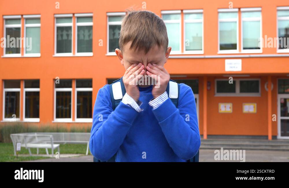 A young boy cries in front of an elementary school in the background ...