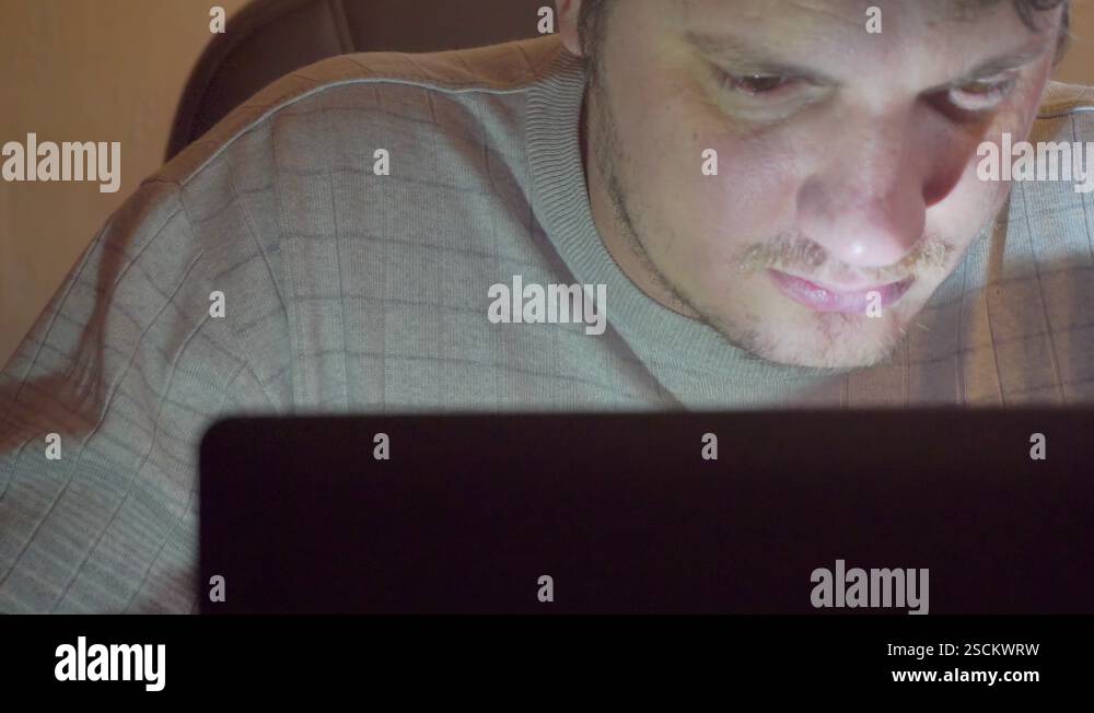 very tired man sitting behind a computer looking at the screen Stock ...