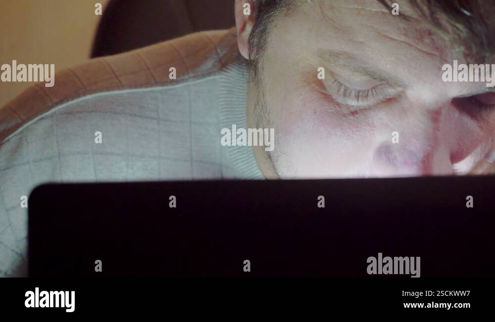 very tired man sitting behind a computer looking at the screen Stock ...