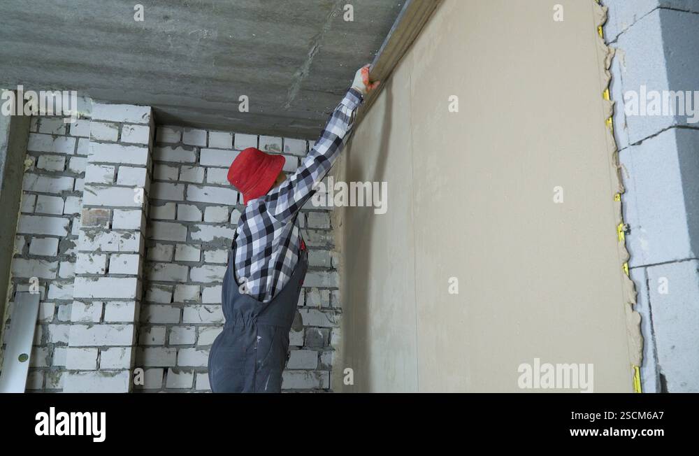 plasterer smoothing plaster on interior wall with construction ruler ...