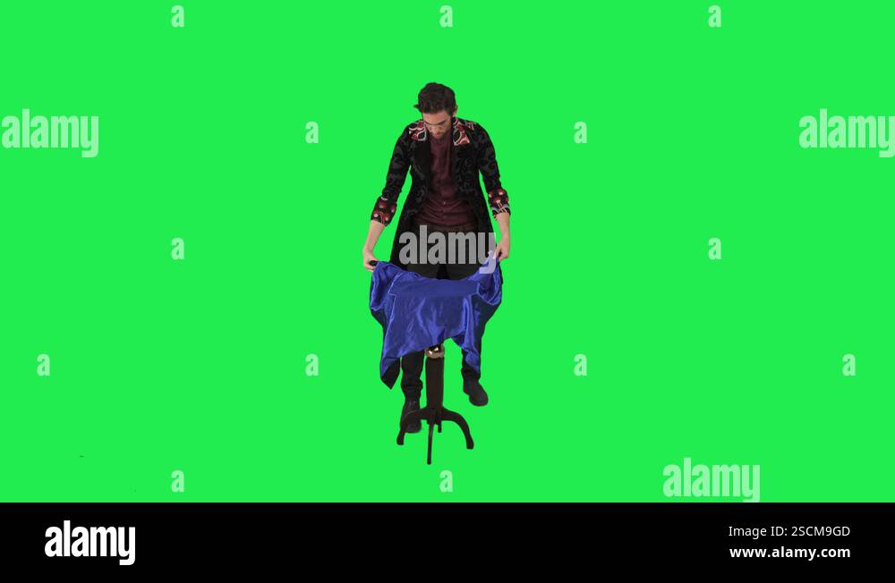 A magician performs a magic trick of a flying table over a green screen ...
