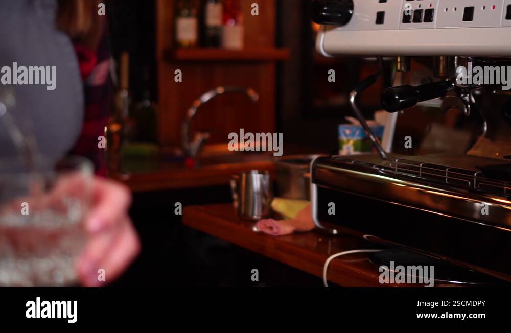 Female barista pouring water in glass placing it on wooden board bar ...