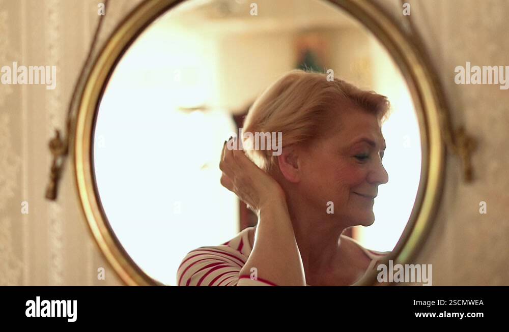 Senior, happy woman checking her look in front of the mirror, slow ...