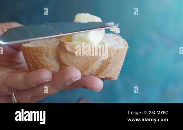 A hand spreads creamy butter on crusty bread in a warm kitchen Stock ...