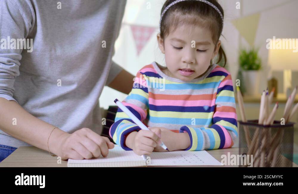Mom teaching her daughter to writing in the book on the table ...