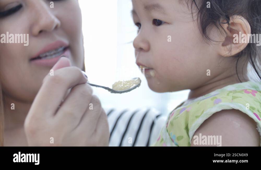 Asian mother feeding food for her daughter at home with smile face ...