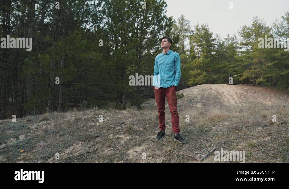 Snappy young man looking around and standing in a pine wood in spring ...