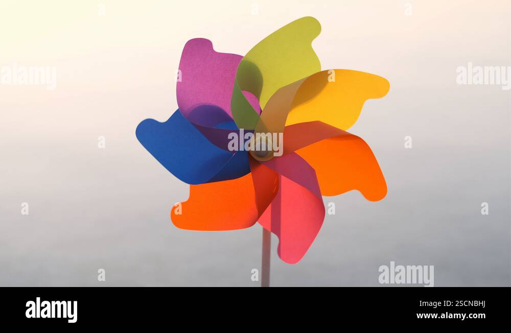 A rotating multi-colored plastic pinwheel with a blowing wind stands on ...