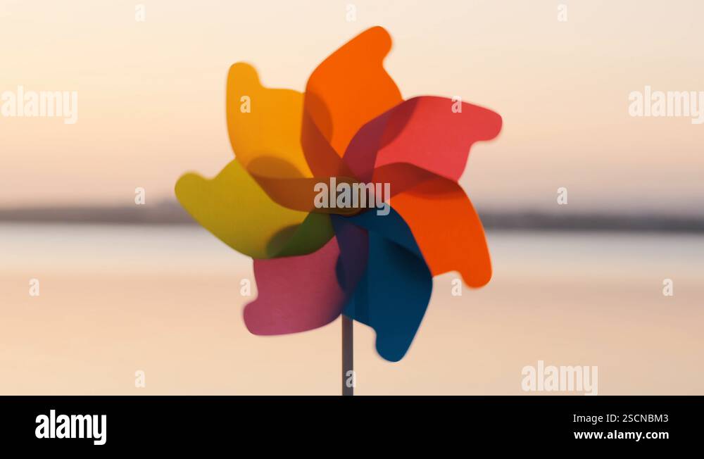 A rotate colored plastic pinwheel with a blowing wind stands on sand by ...
