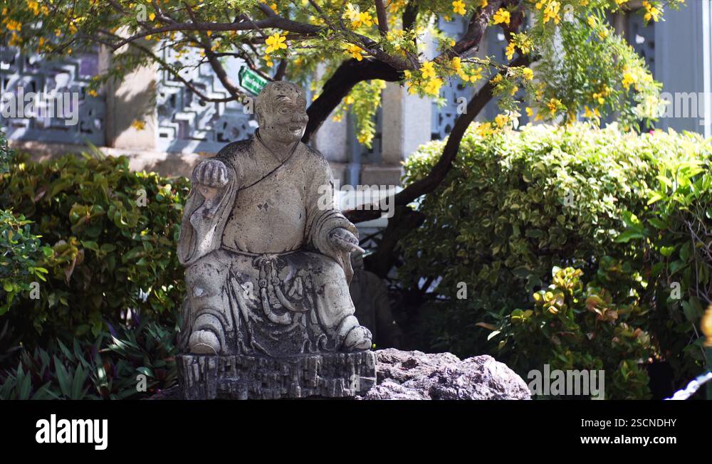 Stone statue of monk under greenn trees in Temple of the Emerald Buddha ...