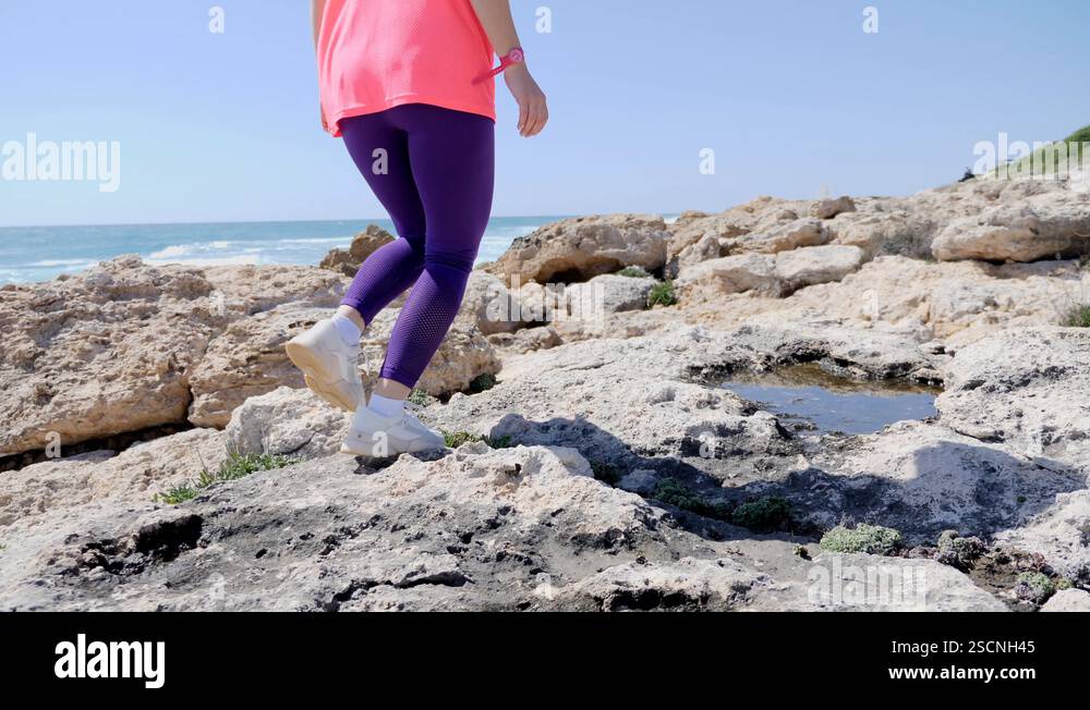 Young fit woman runs the rocky trail along the beach. Trail run on the ...