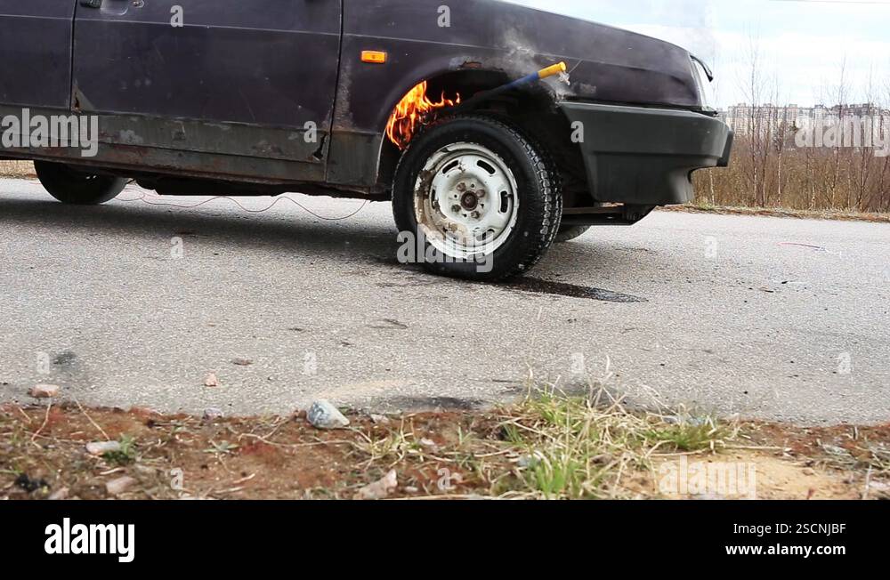 Old violet car is left on abandonded grey road with burning wheel on ...