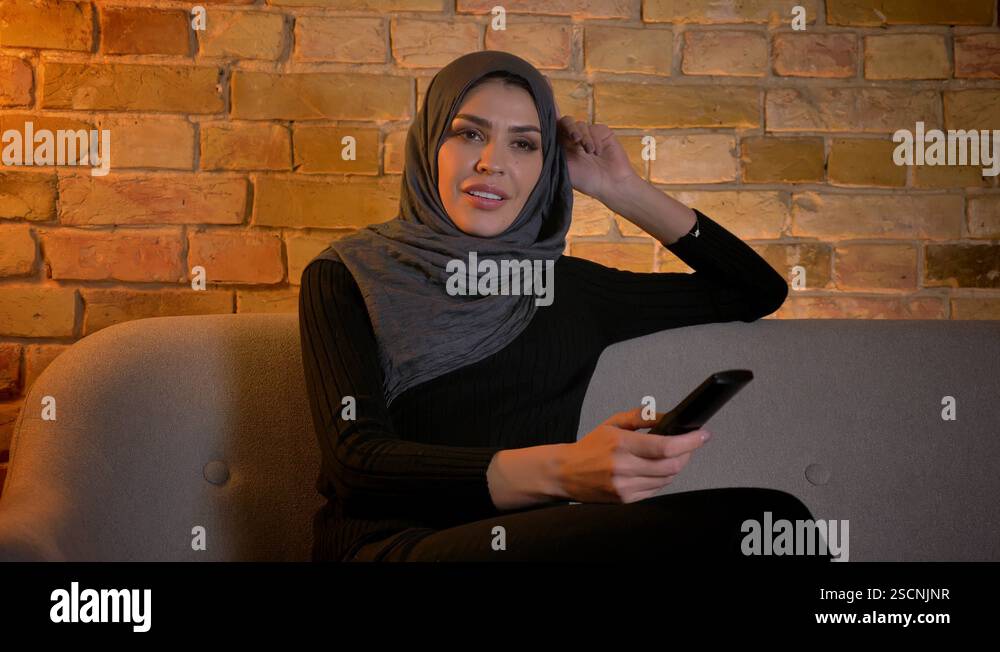 Closeup portrait of adult attractive muslim female in hijab watching TV ...
