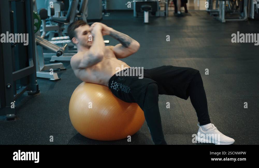 Young muscular man trains abdominal muscles using exercise ball Stock ...