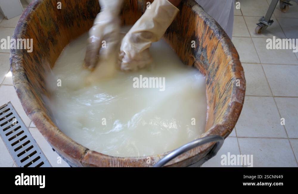 a man works pieces of cheese in a wooden container to prepare Italian ...