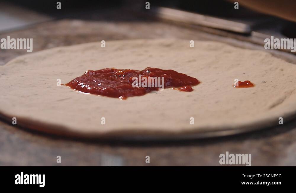 Chef puts tomato sauce on pizza dough with metal spoon in pizzeria ...