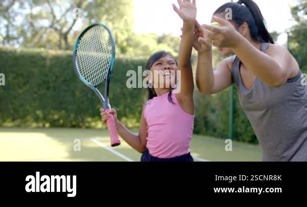 Playing tennis, girl holding racket and making peace sign with woman on ...