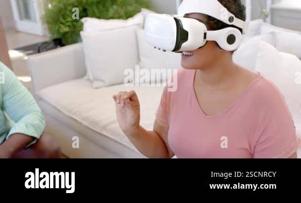 Using VR headset, woman sitting on couch and interacting with virtual environment. Virtual ...