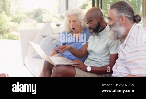 Using laptop, senior friends sitting on couch, discussing something ...