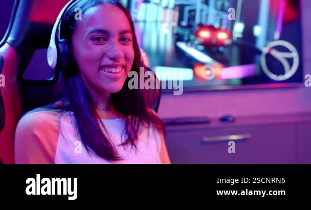 Teenage girl smiling while wearing headphones and playing video game. Gaming, teenage girl ...