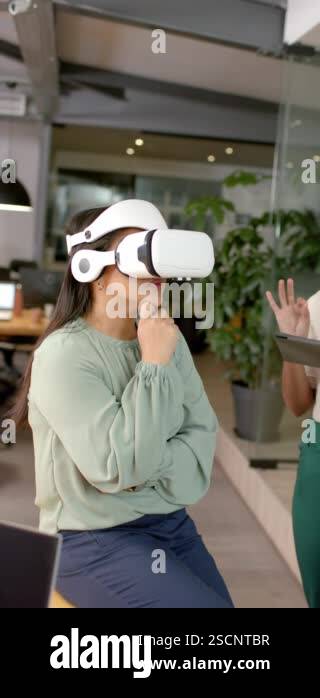 Vertical video: Using VR vr headset, woman interacting with colleague ...
