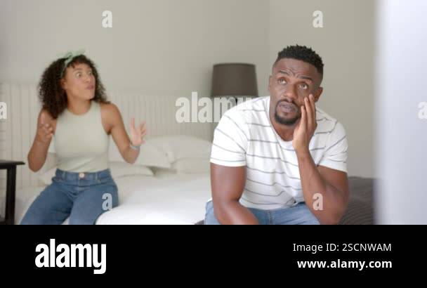 Arguing couple sitting on bed, man rolling eyes and woman gesturing ...