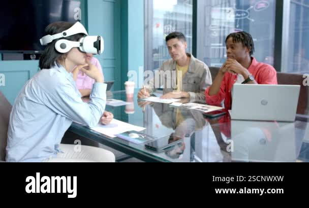 Using VR headset, woman presenting to colleagues with laptops in modern ...