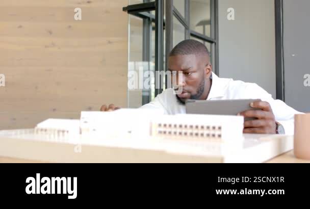 Architect working on building model and using tablet in modern office ...