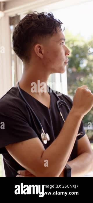 Vertical video: Male nurse with stethoscope looking out window ...