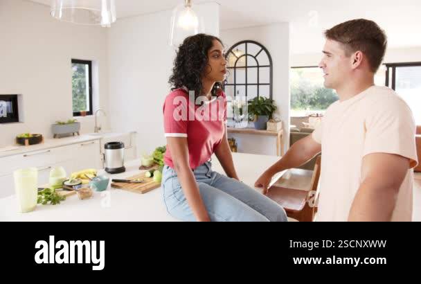 Young multiracial couple sitting on kitchen counter, holding hands and ...