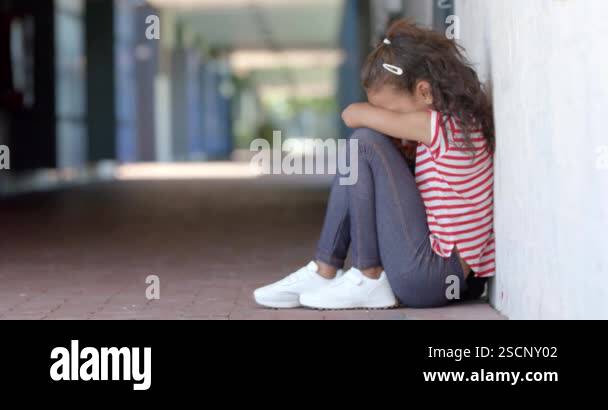 In school, child sitting alone against wall, feeling sad and upset ...