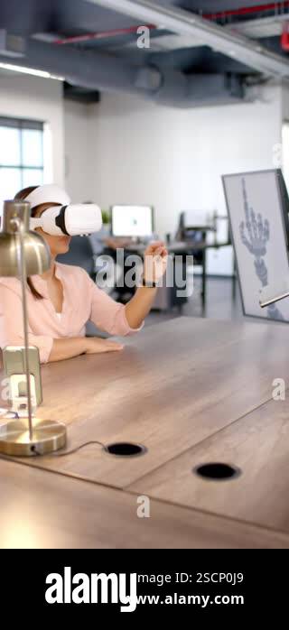 Vertical video: Using VR headset, woman interacting with robotic hand on computer screen in ...